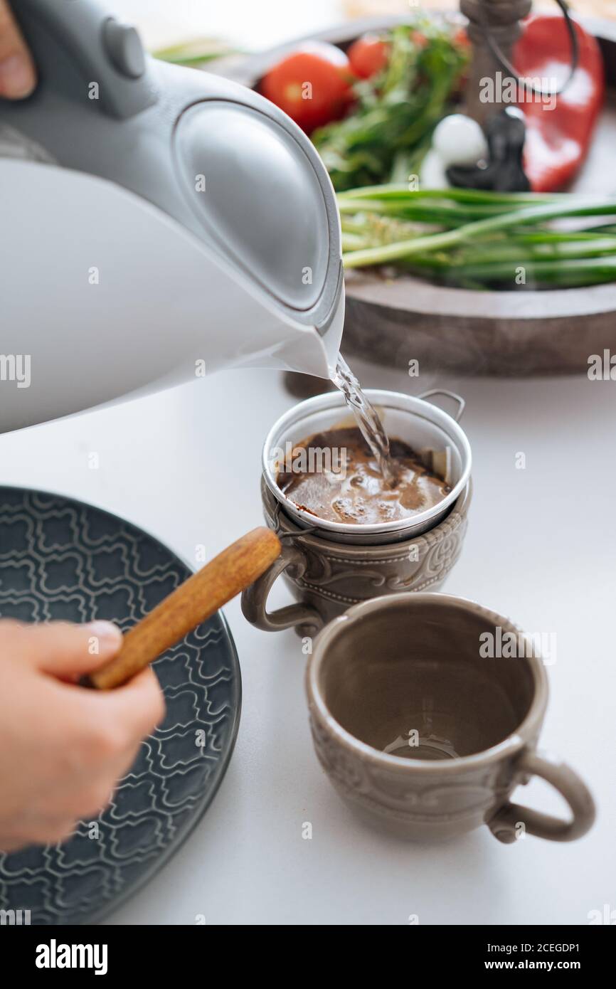 Crop hands pouring hot water from kettle into beautiful ceramic mug ...