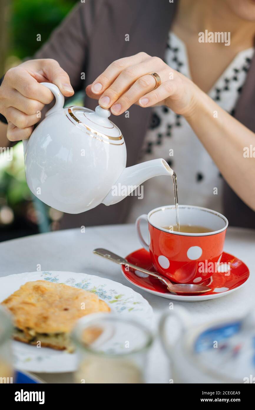 Crop view of female holding porcelain teapot and pouring hot tea into ...