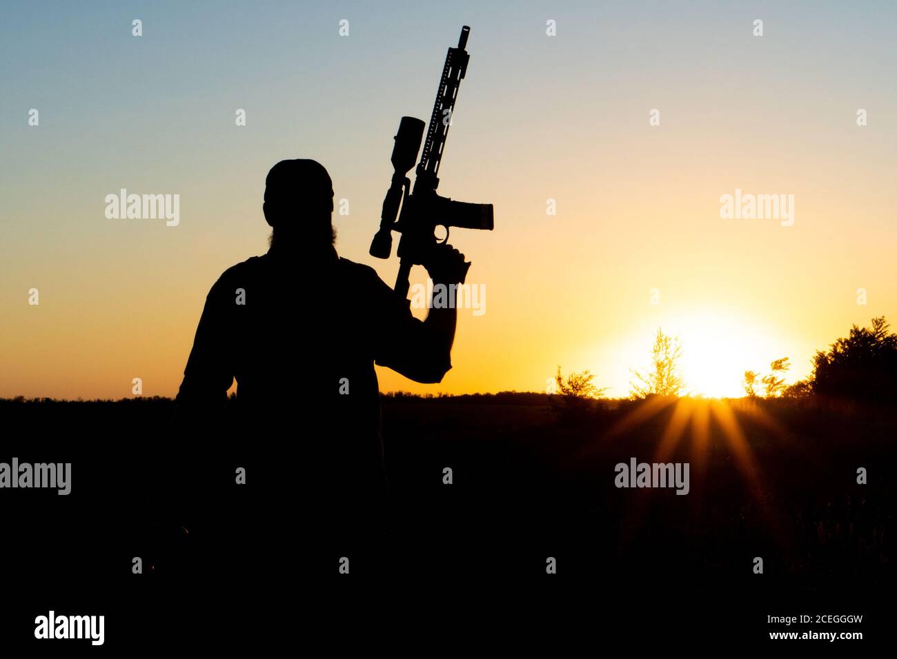 Silhouette of a man with a weapon in his hands on a sunset background ...