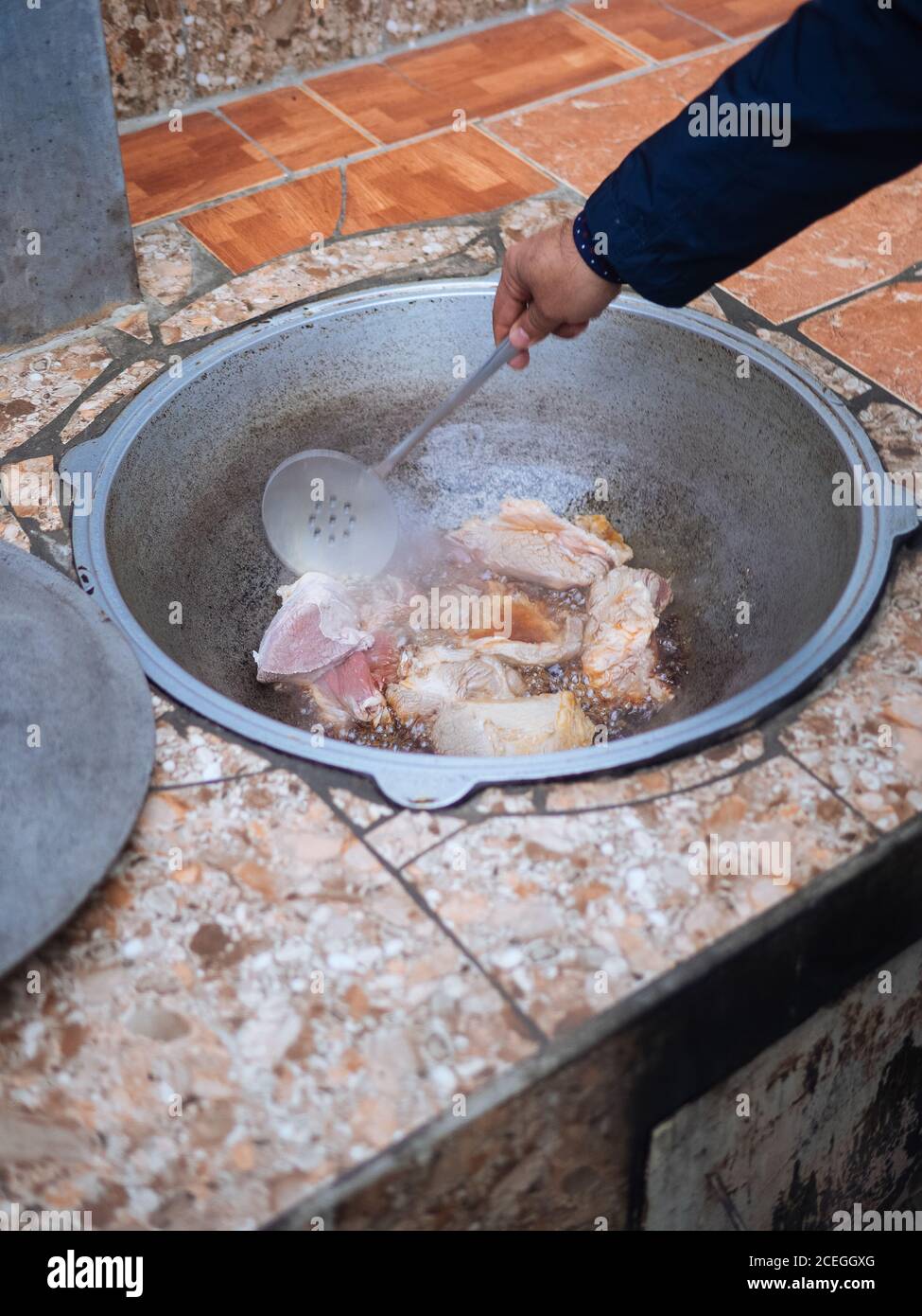 Crop person frying large chunks of meat in oil inside of metal cauldron ...