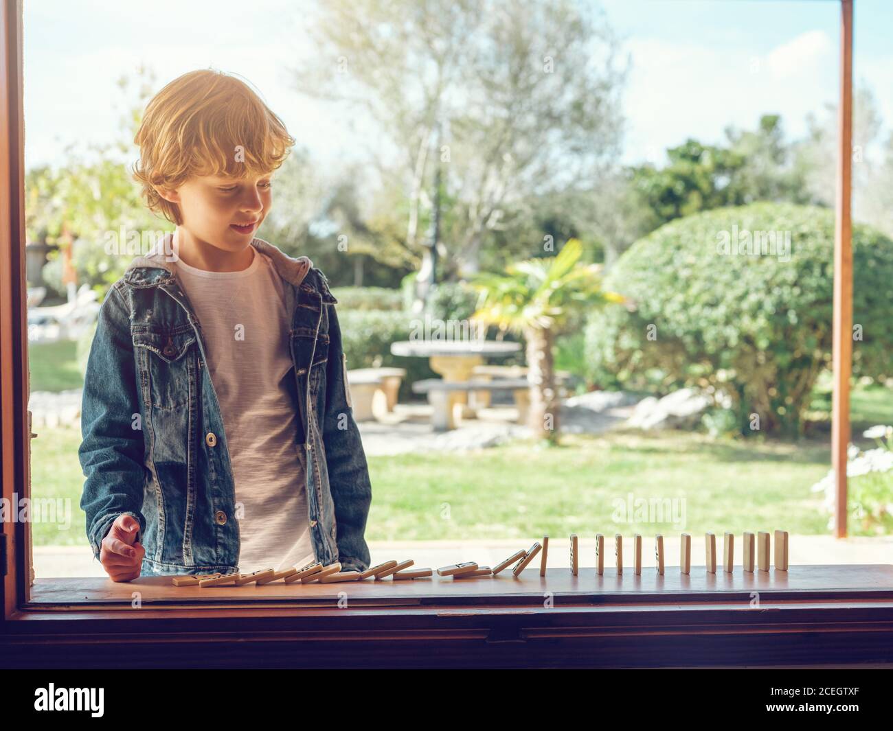 Adorable young boy standing at the window and playing with falling ...