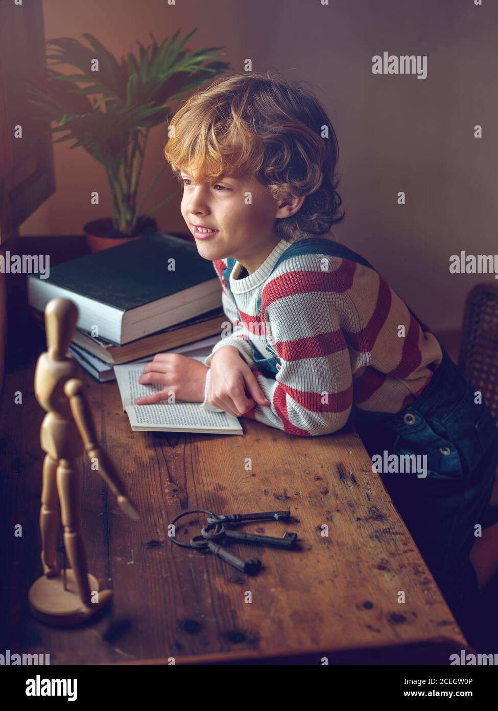 Side view of young boy sitting at wooden vintage table and looking away ...