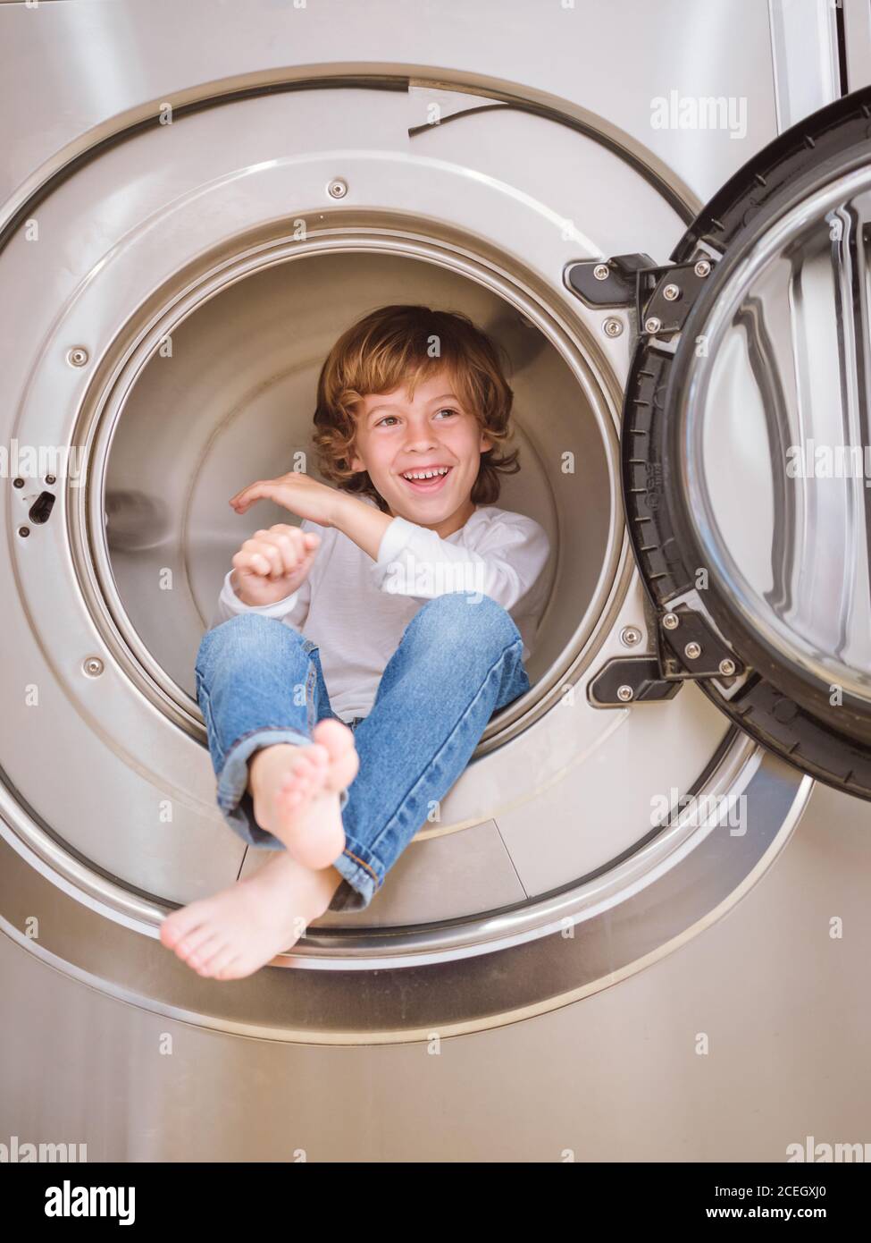 Cute young boy sitting inside the washing machine and looking at camera ...