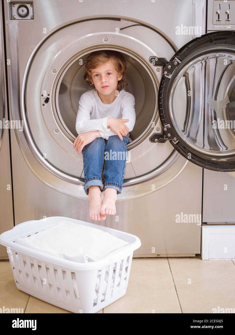 Cute young boy sitting inside the washing machine and looking at camera ...