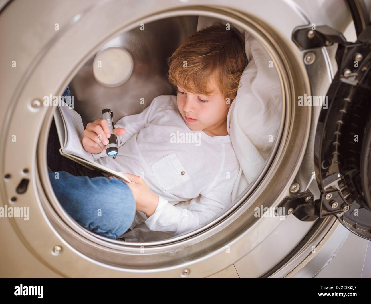 Young boy with flashlight lying inside the washing machine and reading ...