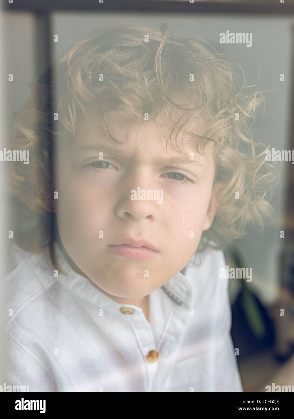 Close-up view of cute blond kid with curly hair in white shirt quietly ...