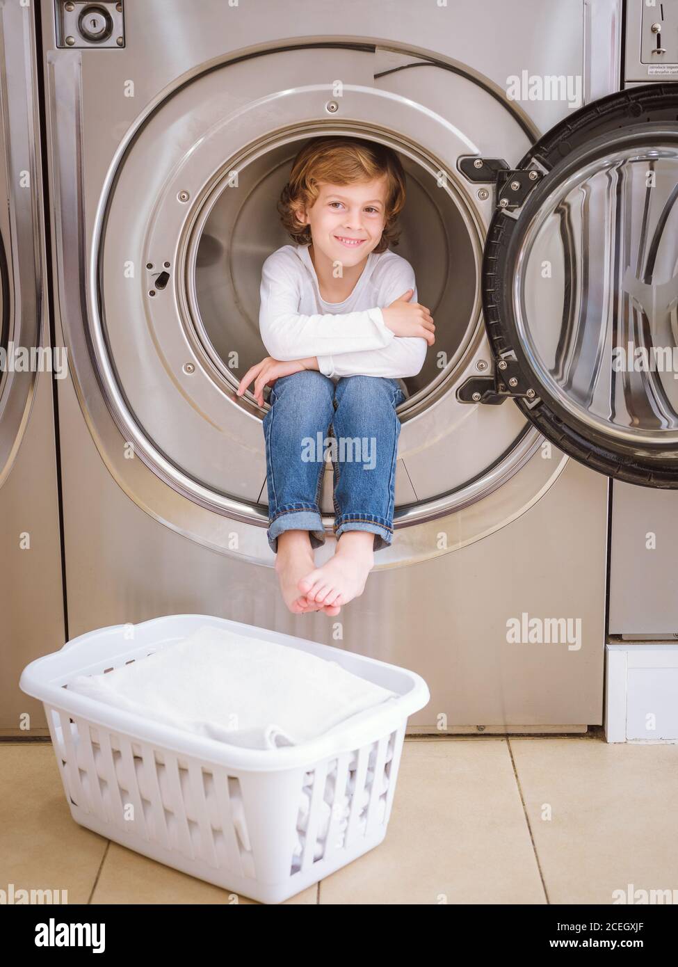 Cute young boy sitting inside the washing machine and looking at camera ...