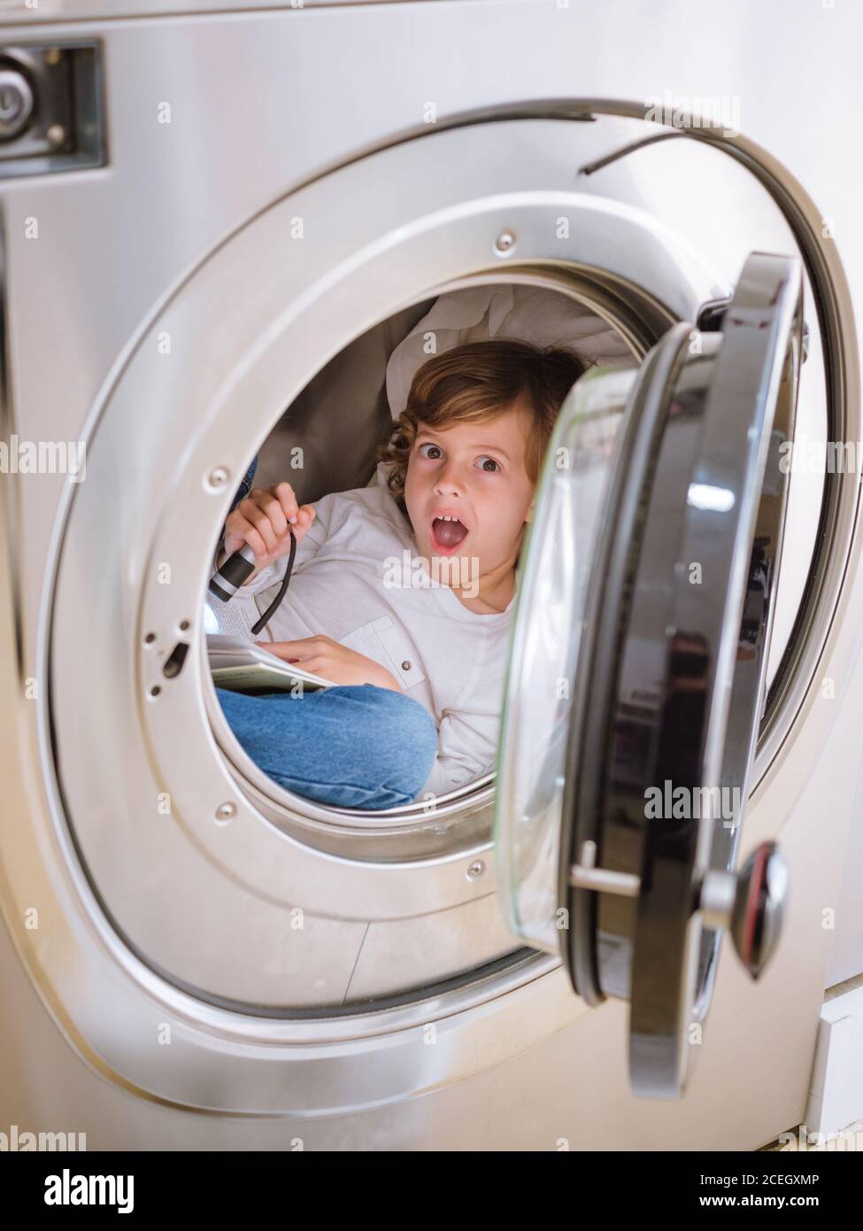 Young boy with flashlight lying inside the washing machine and reading ...
