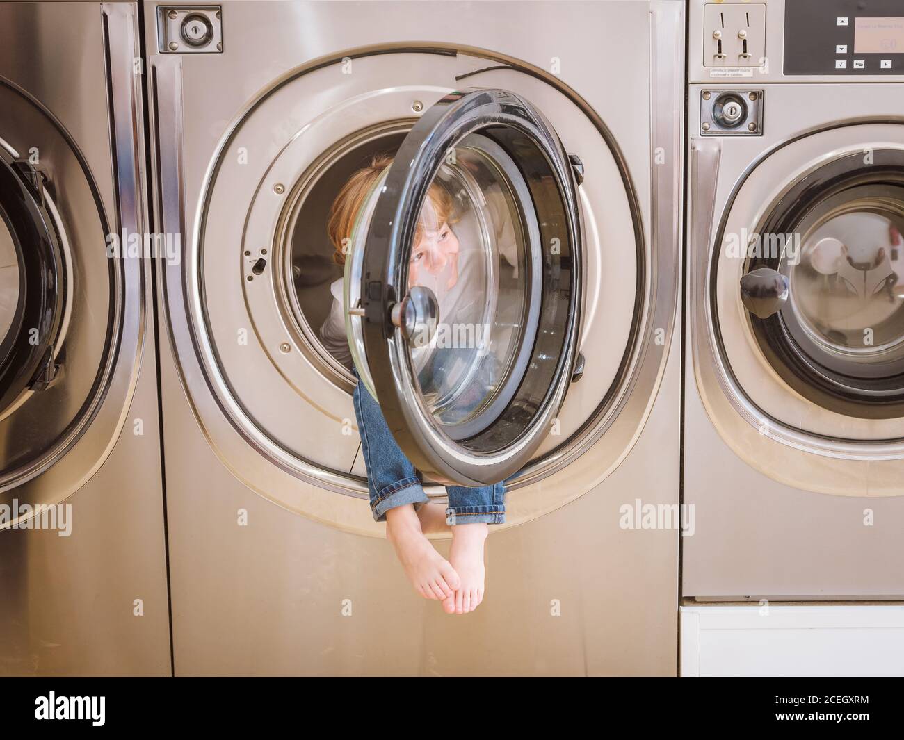 Adorable curious boy sitting inside the washing machine in the laundry ...