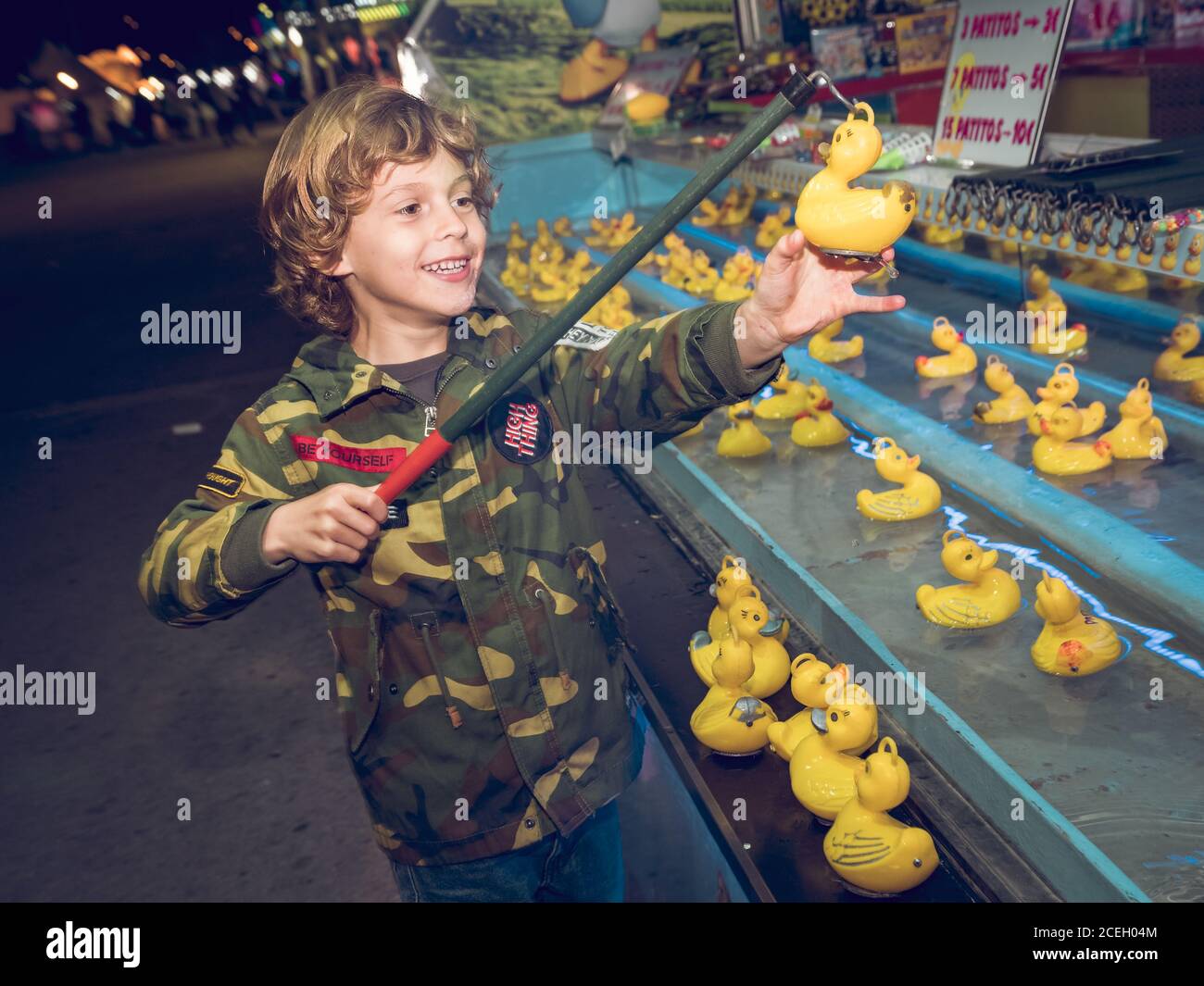 Side view of cheerful boy standing at attraction and catching duck toys ...