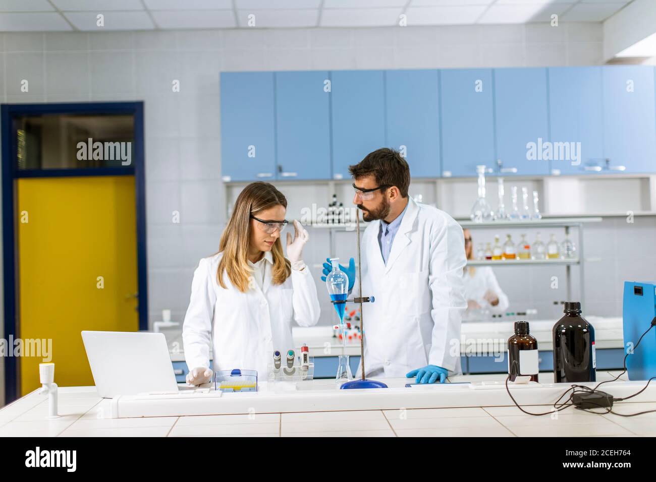 Researchers working with blue liquid at separatory funnel in the ...