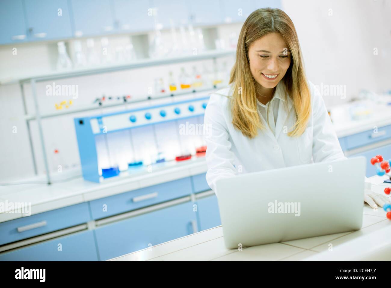 Cute female researcher in white lab coat using laptop while working in ...