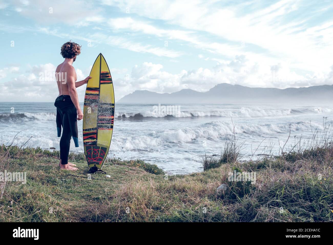 Side view guy standing with bright surf board on coast near ocean with ...