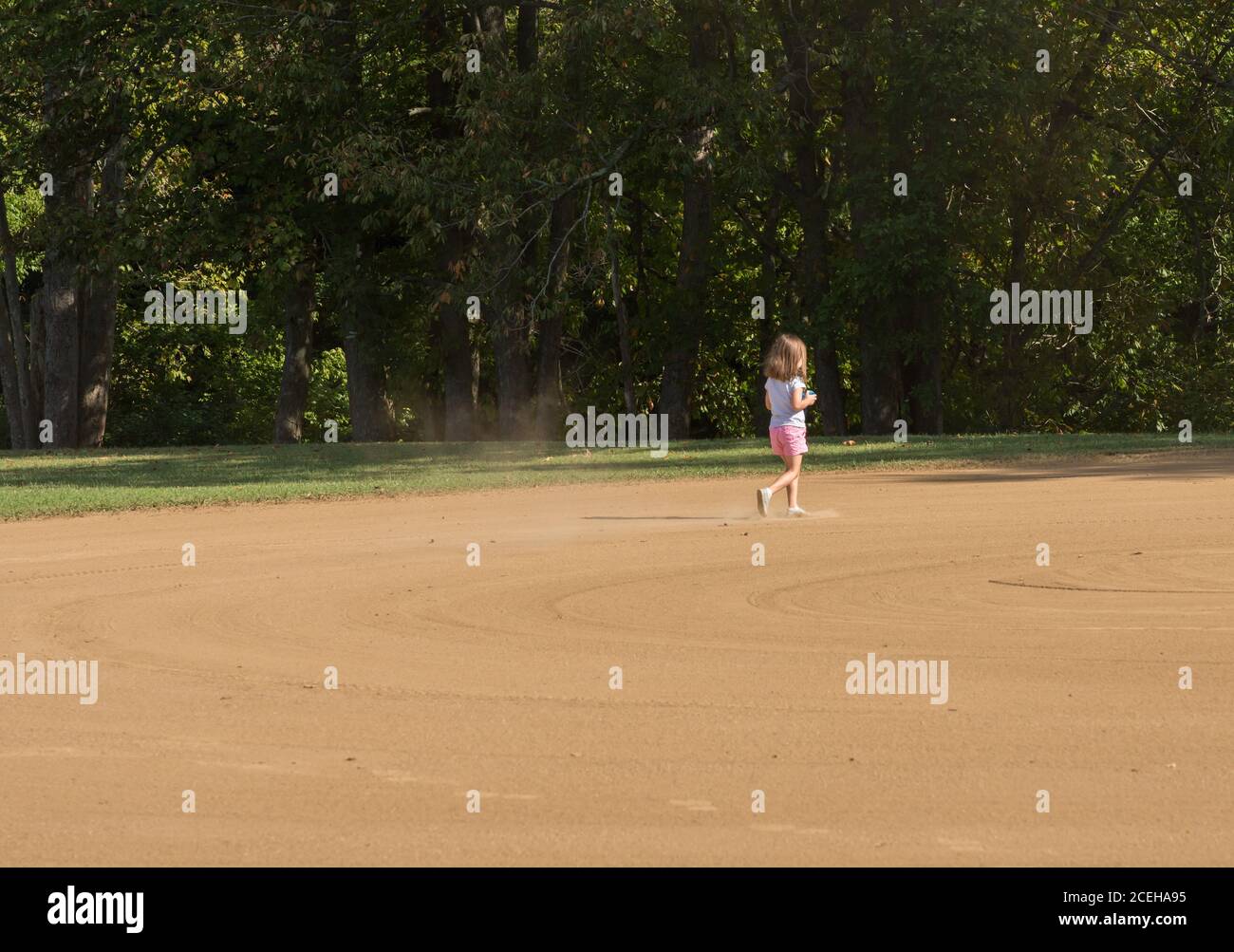 Small toddler girl playing in the sand and dirt of an empty baseball ...