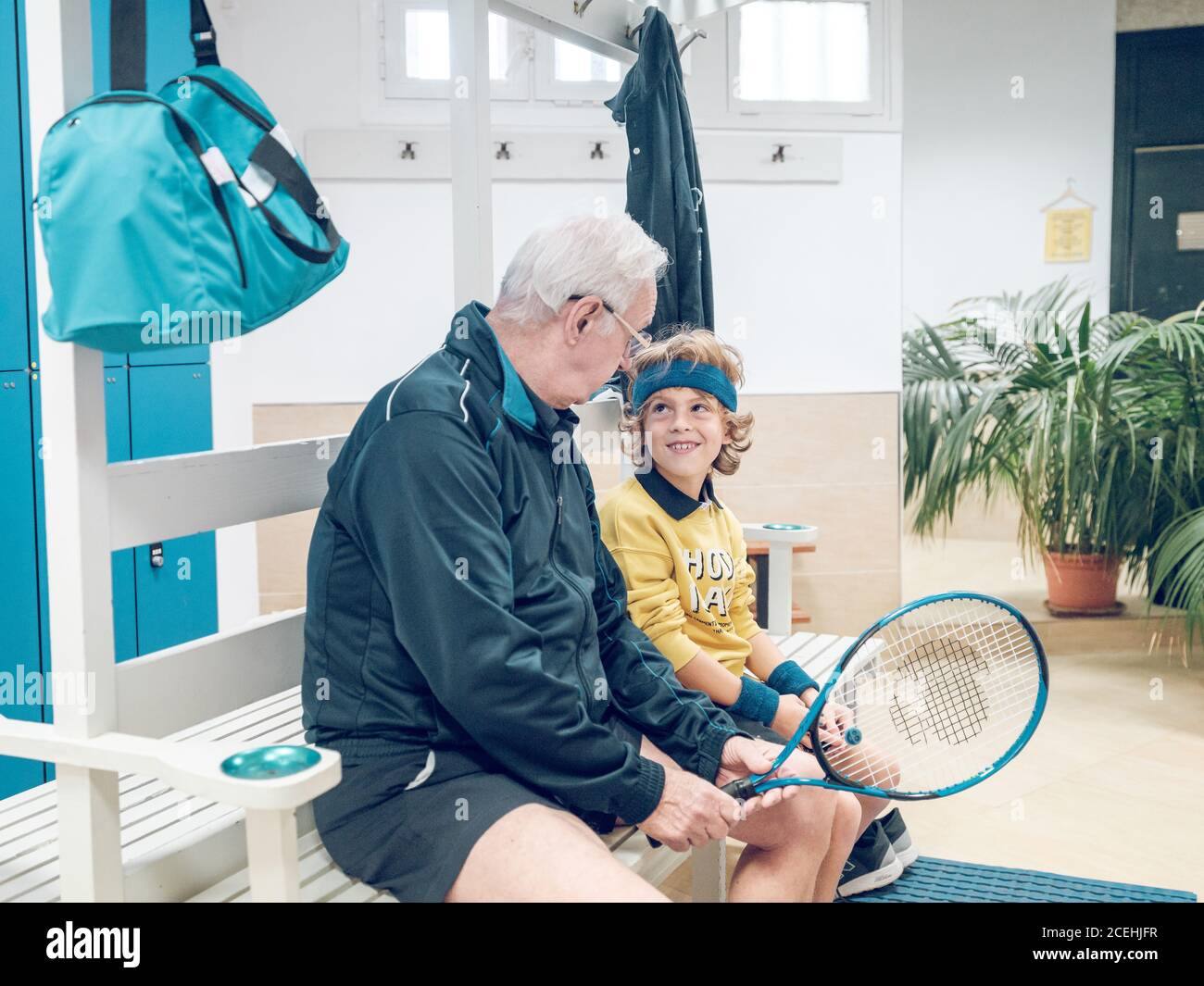 Side view aged grey male in sportswear showing tennis racket to little ...