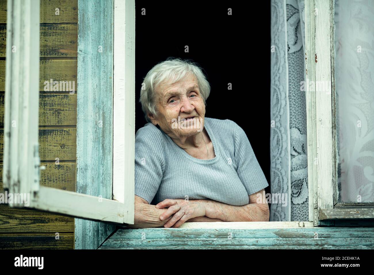 An old woman looks out the window of a village house Stock Photo - Alamy