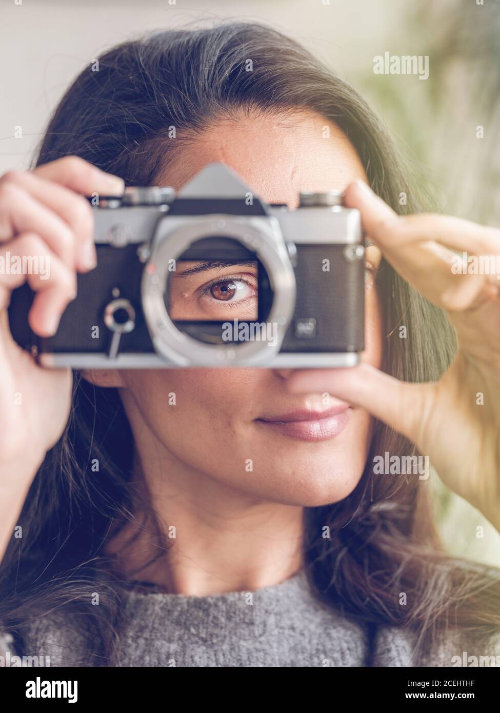 Beautiful adult female looking at camera trough retro camera without ...