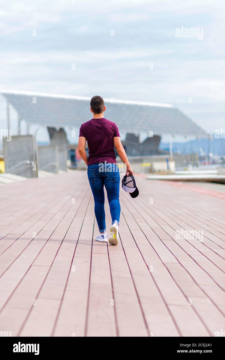 Back view of contemporary casual teenage man in denim carrying cap and ...