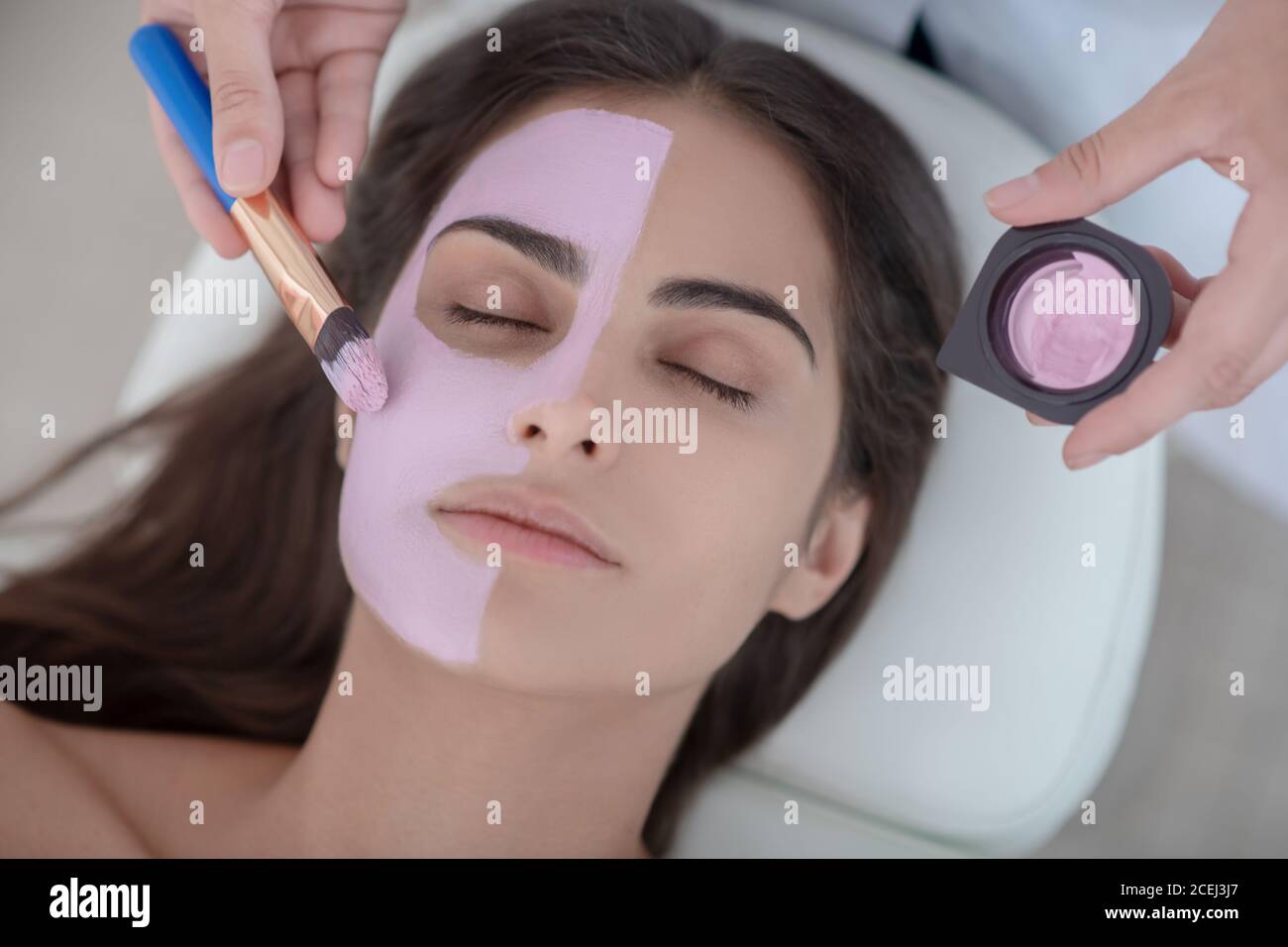 Cosmetologist applying pink facial mask on womans face Stock Photo - Alamy