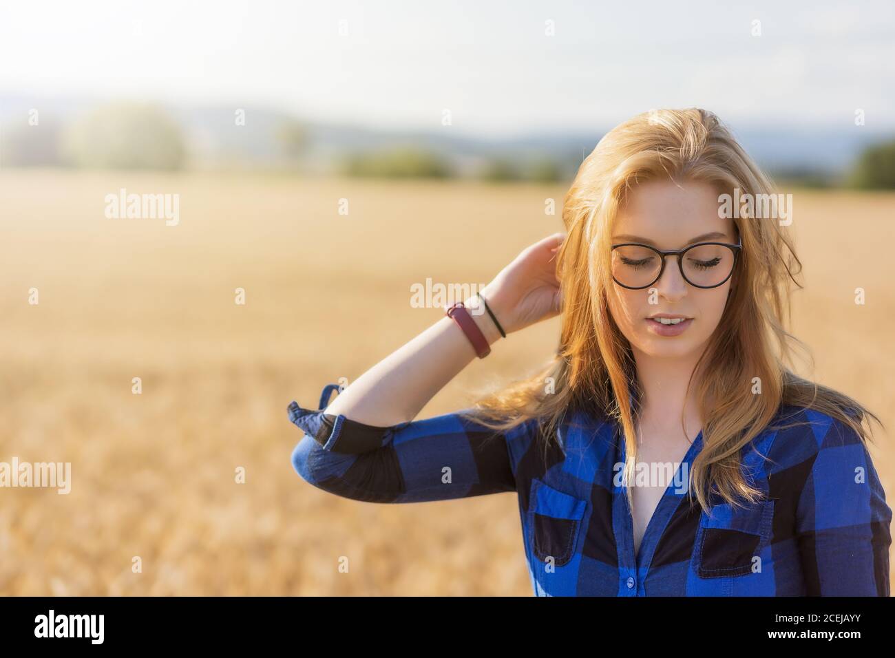 Portrait of cool young woman holding one hand in her hair in corn field ...