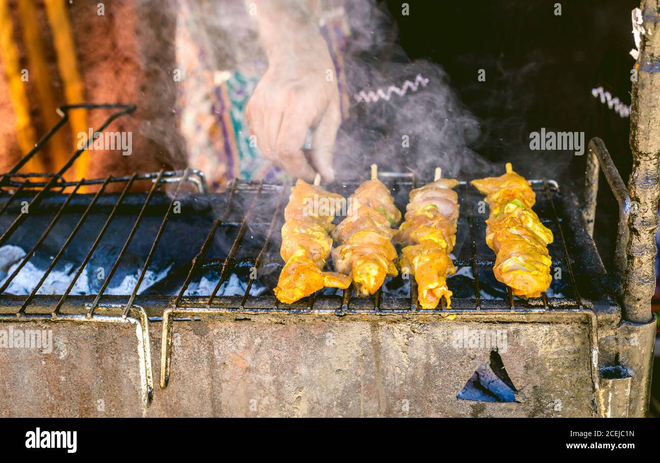 Crop unrecognizable person turning skewered meat while cooking on grill ...