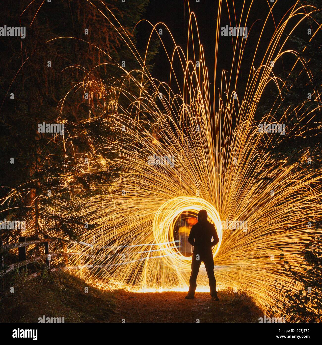 Back view of man standing in dark park with bright flames with long ...