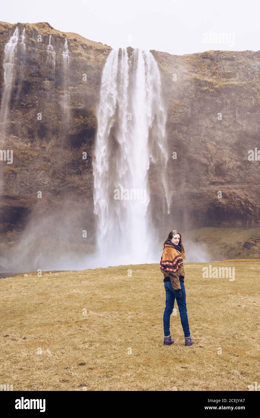 Back view young lady on field near water cascade falling in river ...