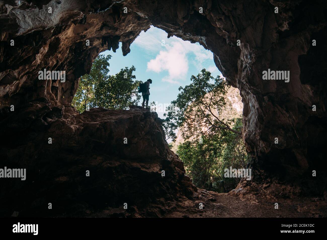 View from inside of rocky cave of person standing on rock on background ...