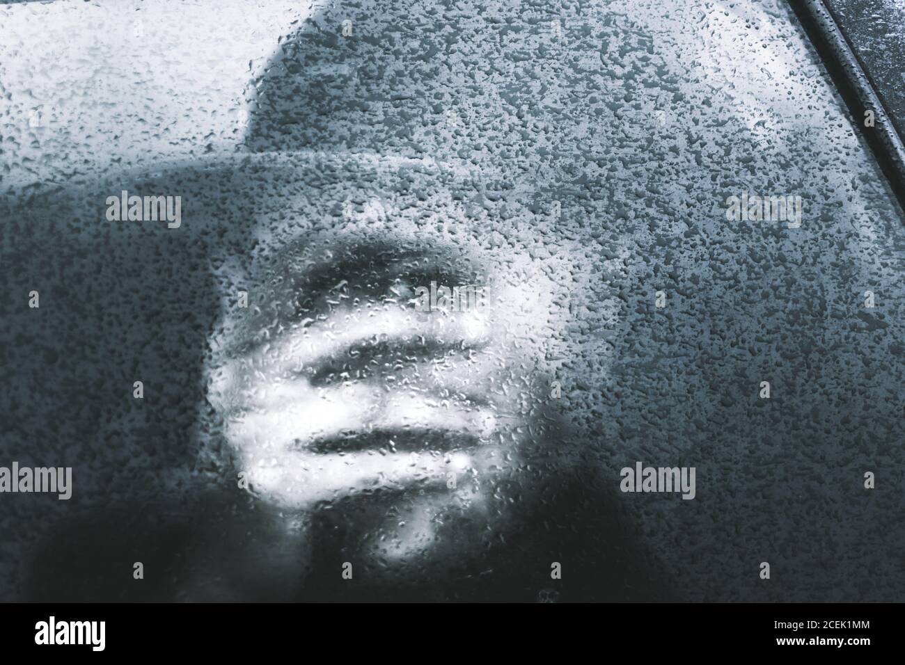 Silhouette of human in cap closing face by hand inside of car window ...