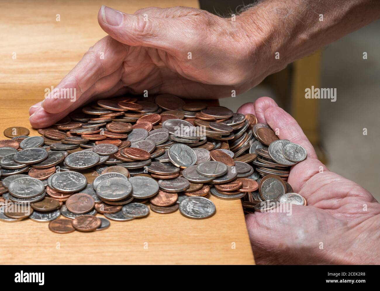 Hundreds of US coins being gathered into hands on wooden table as ...