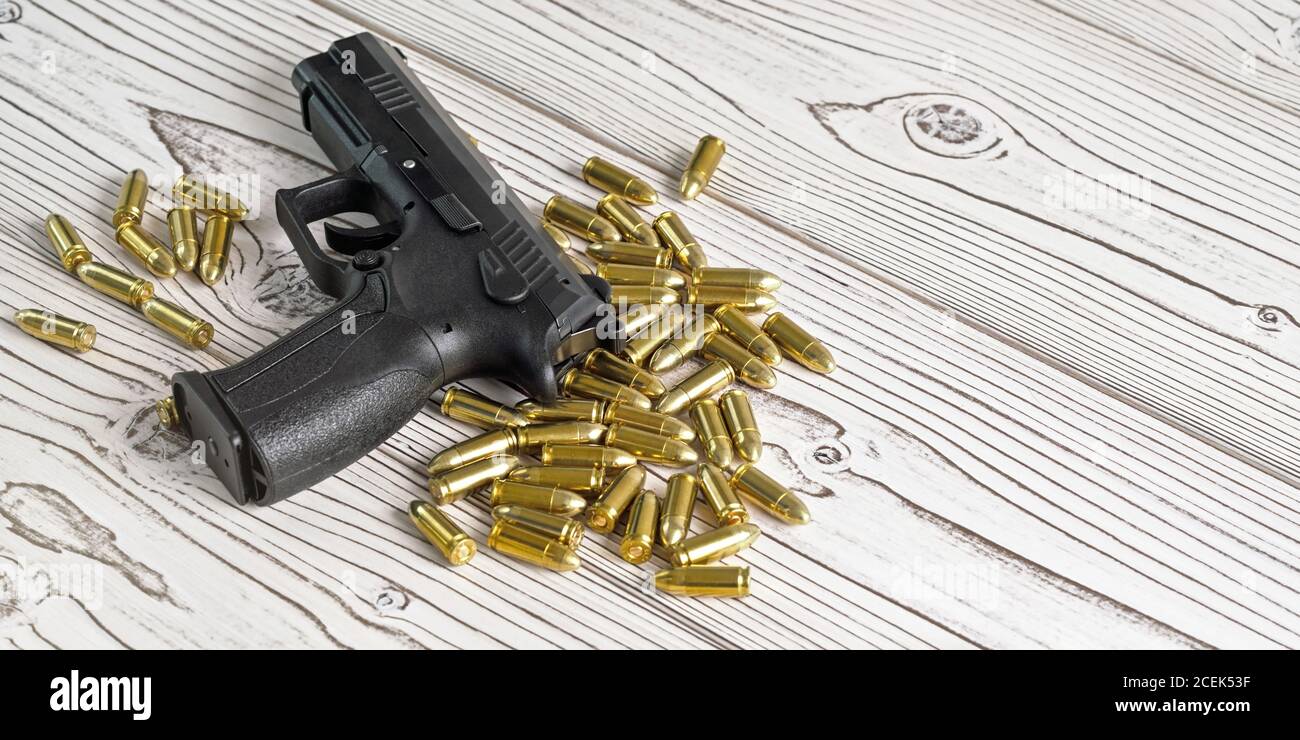 Black metal gun and brass yellow bullets scattered on white boards ...