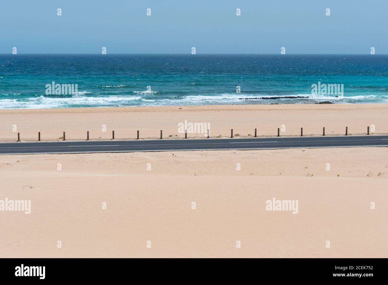 Fenced highway on sandy plain with coast on endless blue wavy ocean ...
