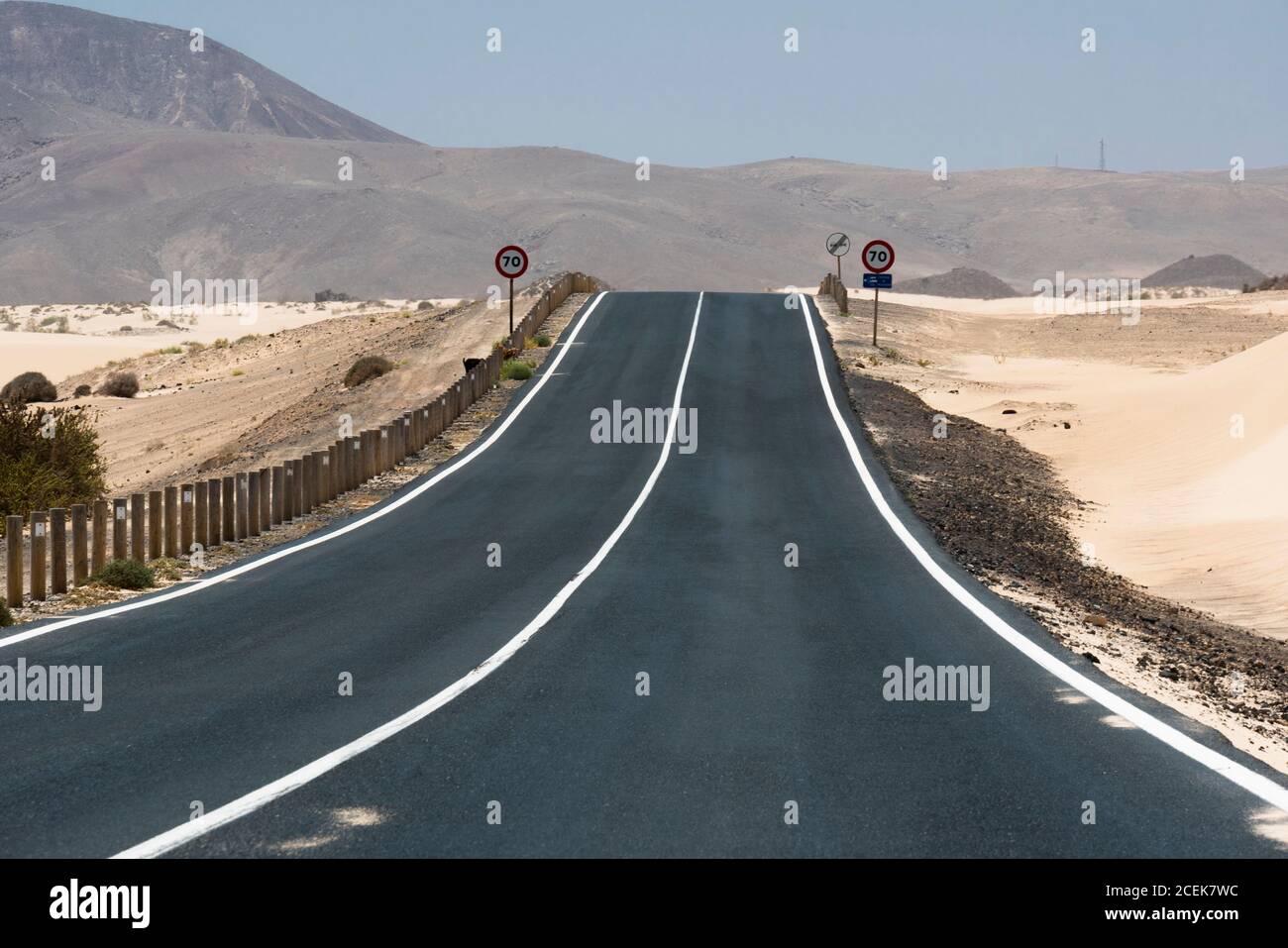Clean straight road with signs on dry sandy plain with hills and ...