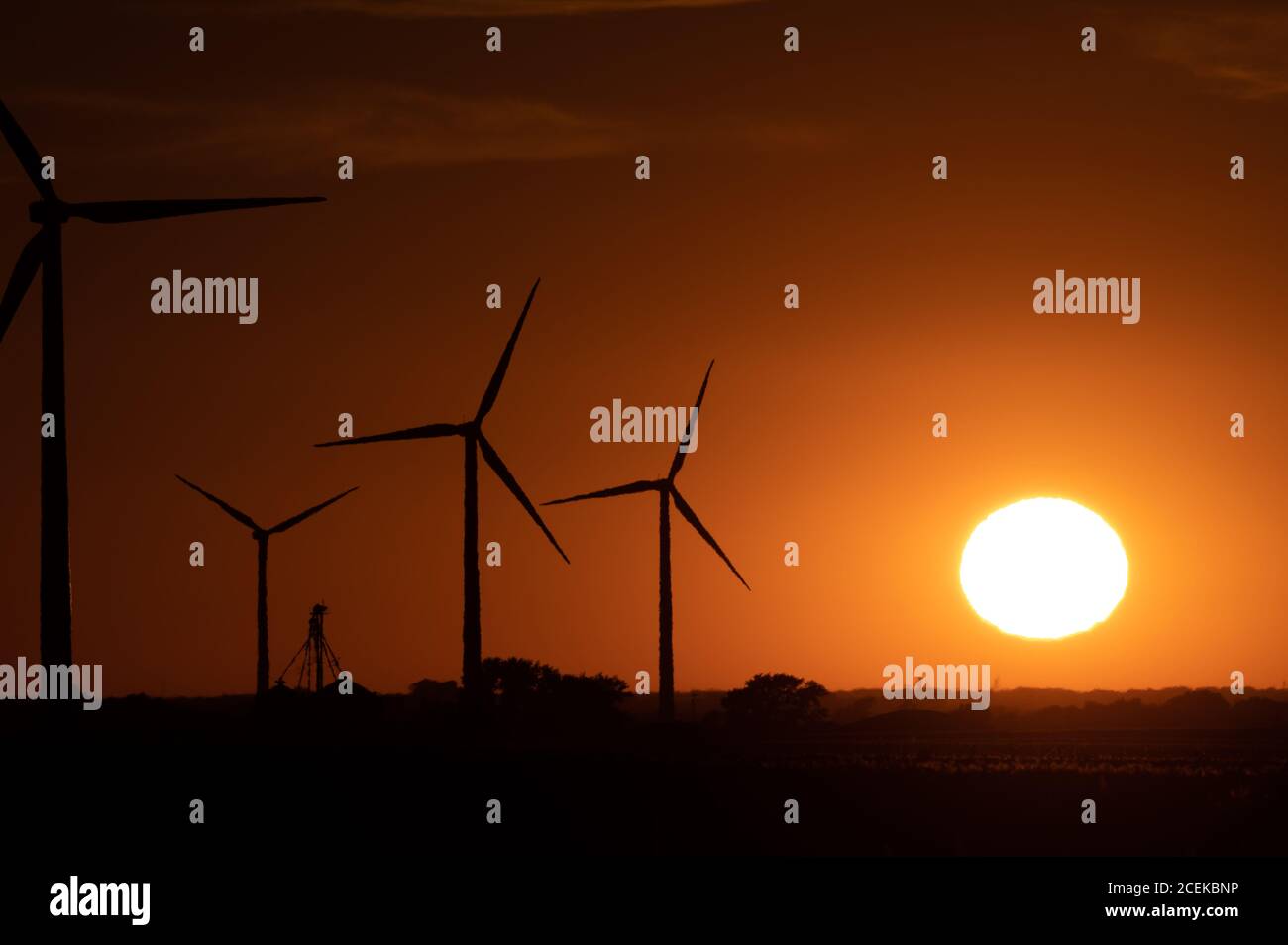 The sun sets behind a group of wind turbines in a wind farm in the ...