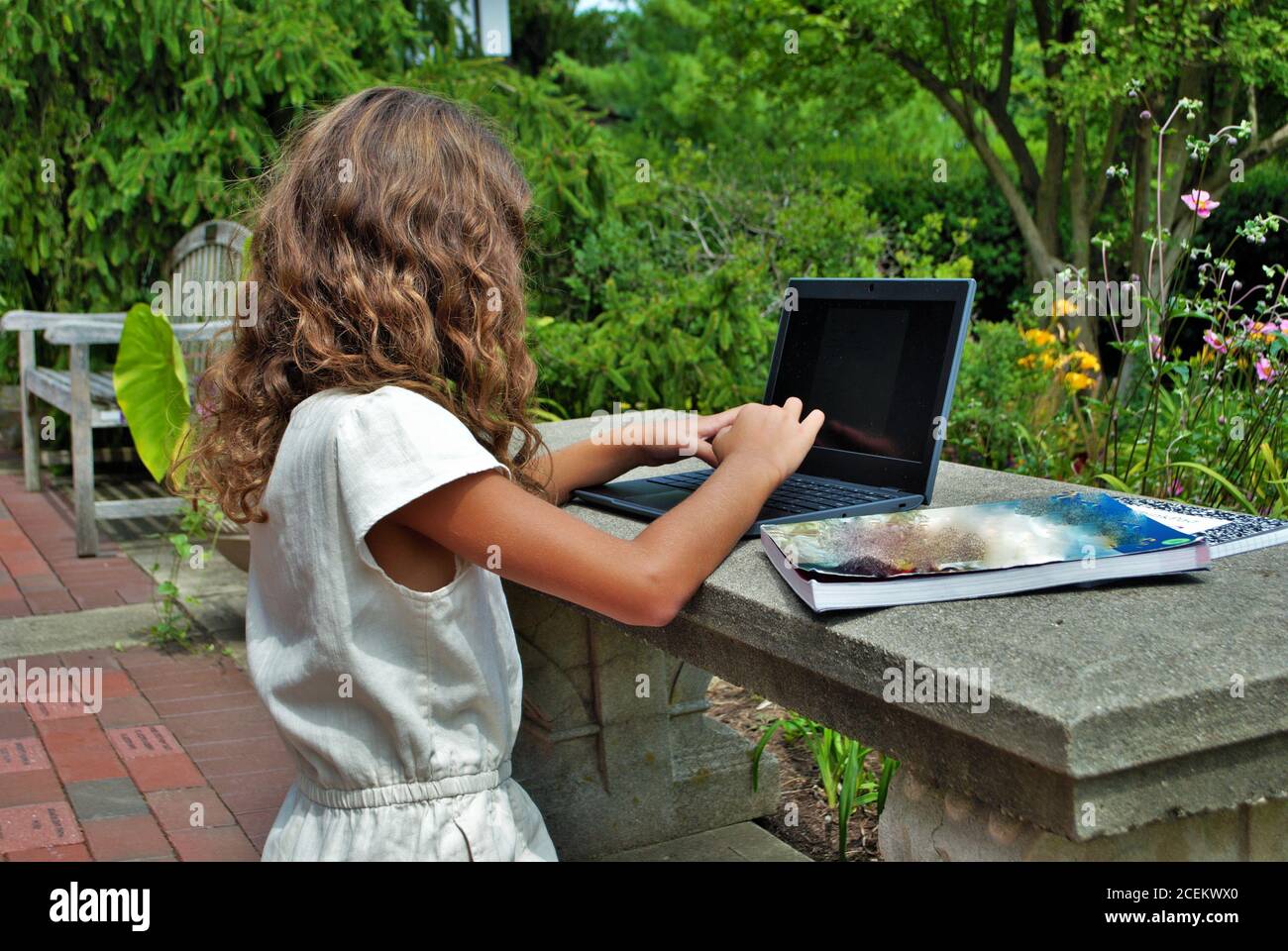 young girl doing school work on a computer remote learning in the park ...
