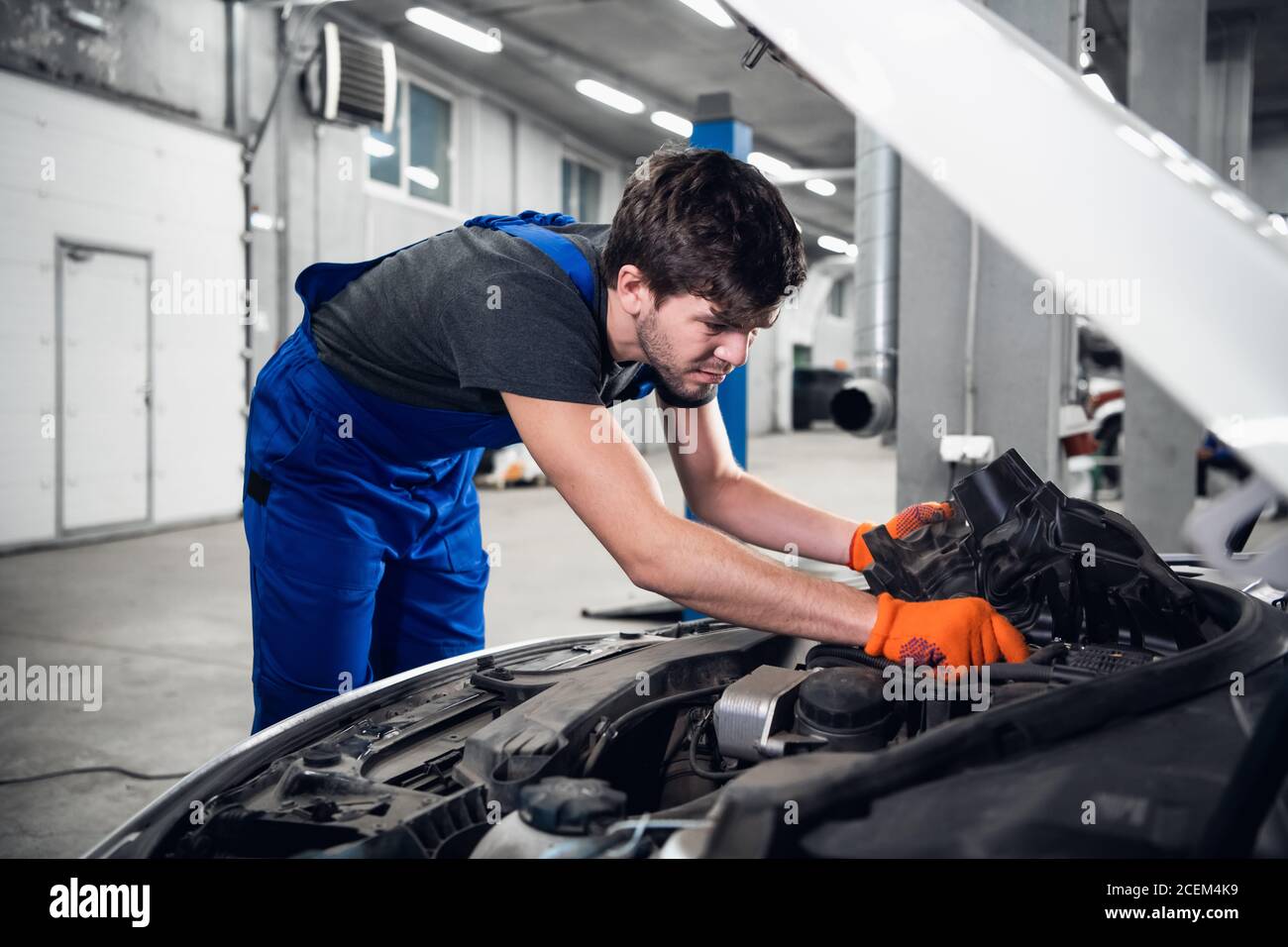 A man is fixing a car engine. He is dressed in overalls and gloves ...