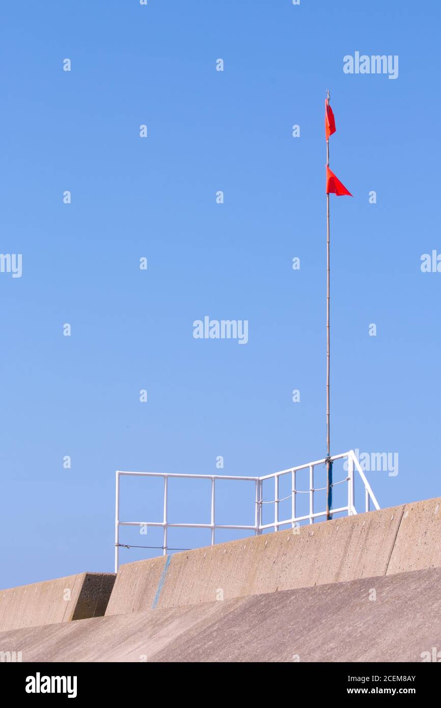 Red flags mark beach access on top of a coastal protection barrier ...