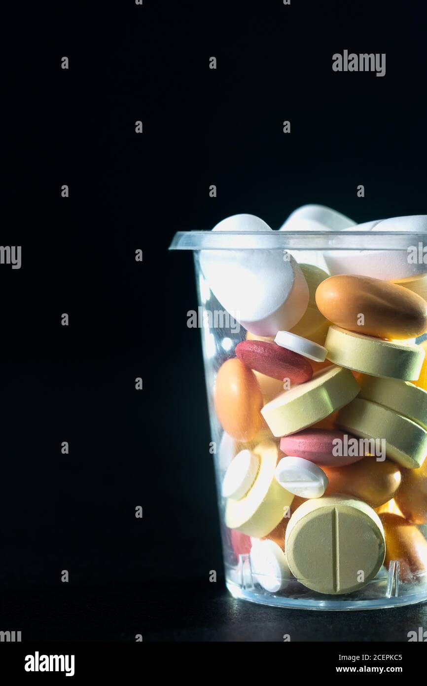 Vertical shot of pharmaceuticals pills and antibiotics in a plastic cup ...
