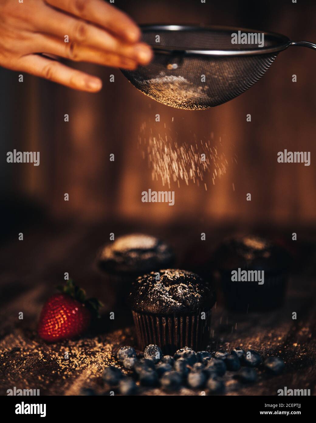 Person pouring sugar powder on a chocolate cupcake through a strainer ...