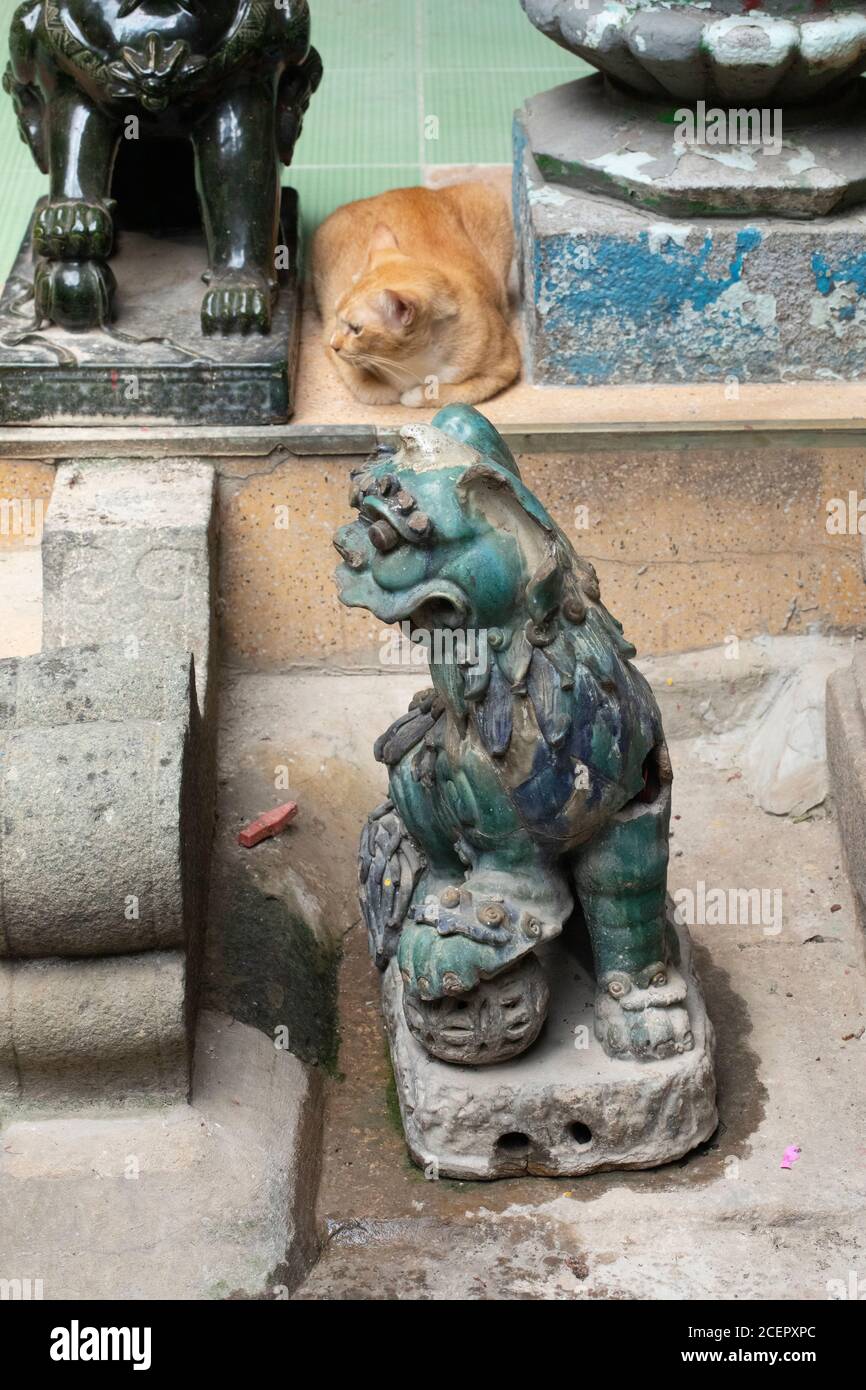 A Ginger cat sitting between statues of cats in an old Chinese Buddhist ...