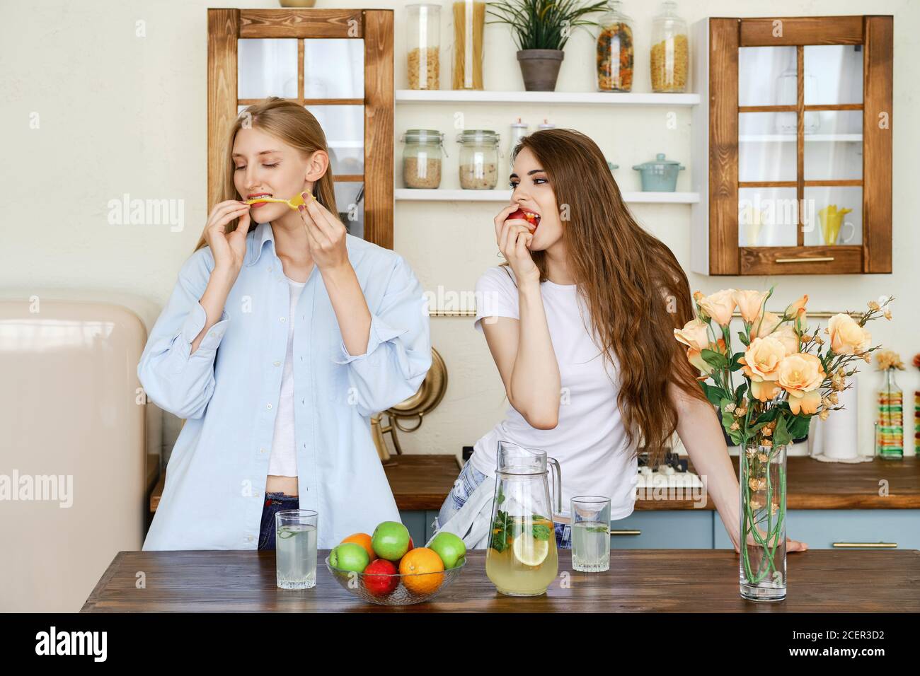 Two beautiful young women eat fruits in the kitchen Stock Photo - Alamy