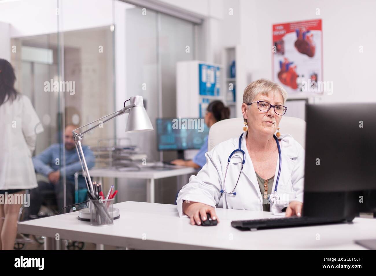 Elderly aged woman doctor working on pc in hospital office, Young ...