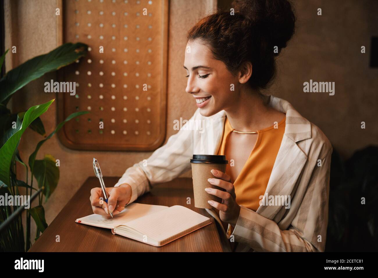 Image of a happy young business woman indoors in cafe drinking coffee ...