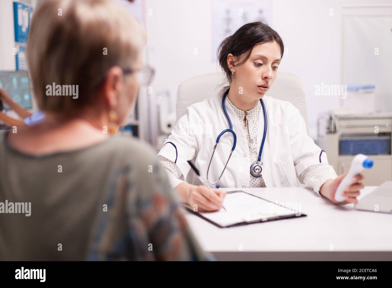 Medic writing senior patient diagnosis after measuring body temperature ...
