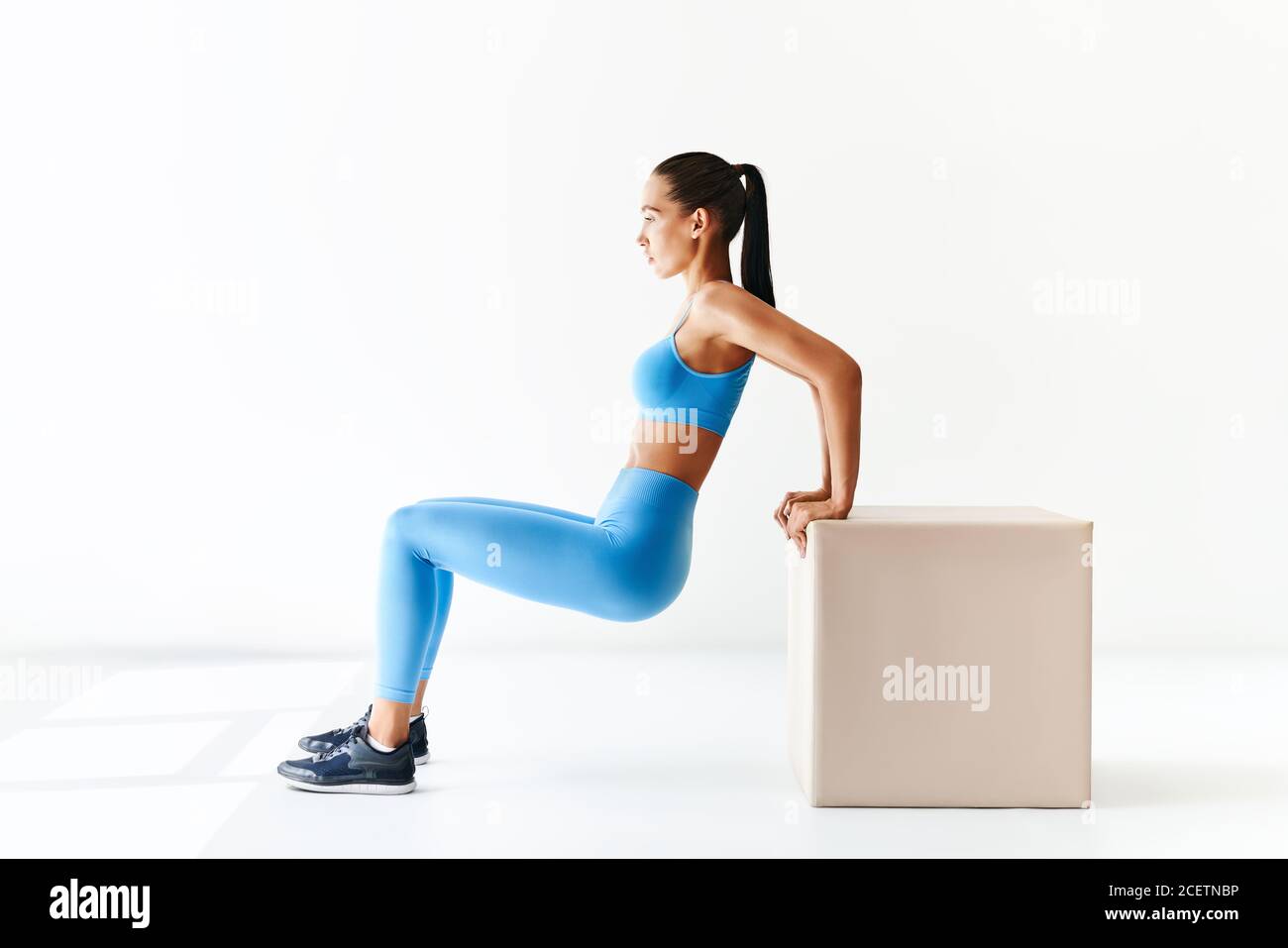 Sporty woman practicing squat exercises with big cube over white ...