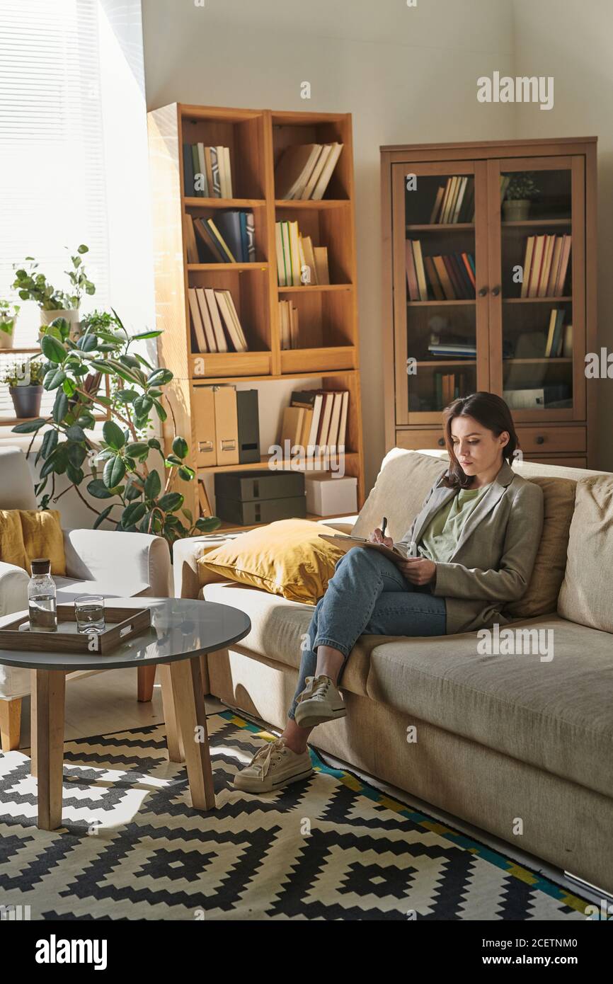 Young woman sitting on comfartable sofa in modern office room holding ...