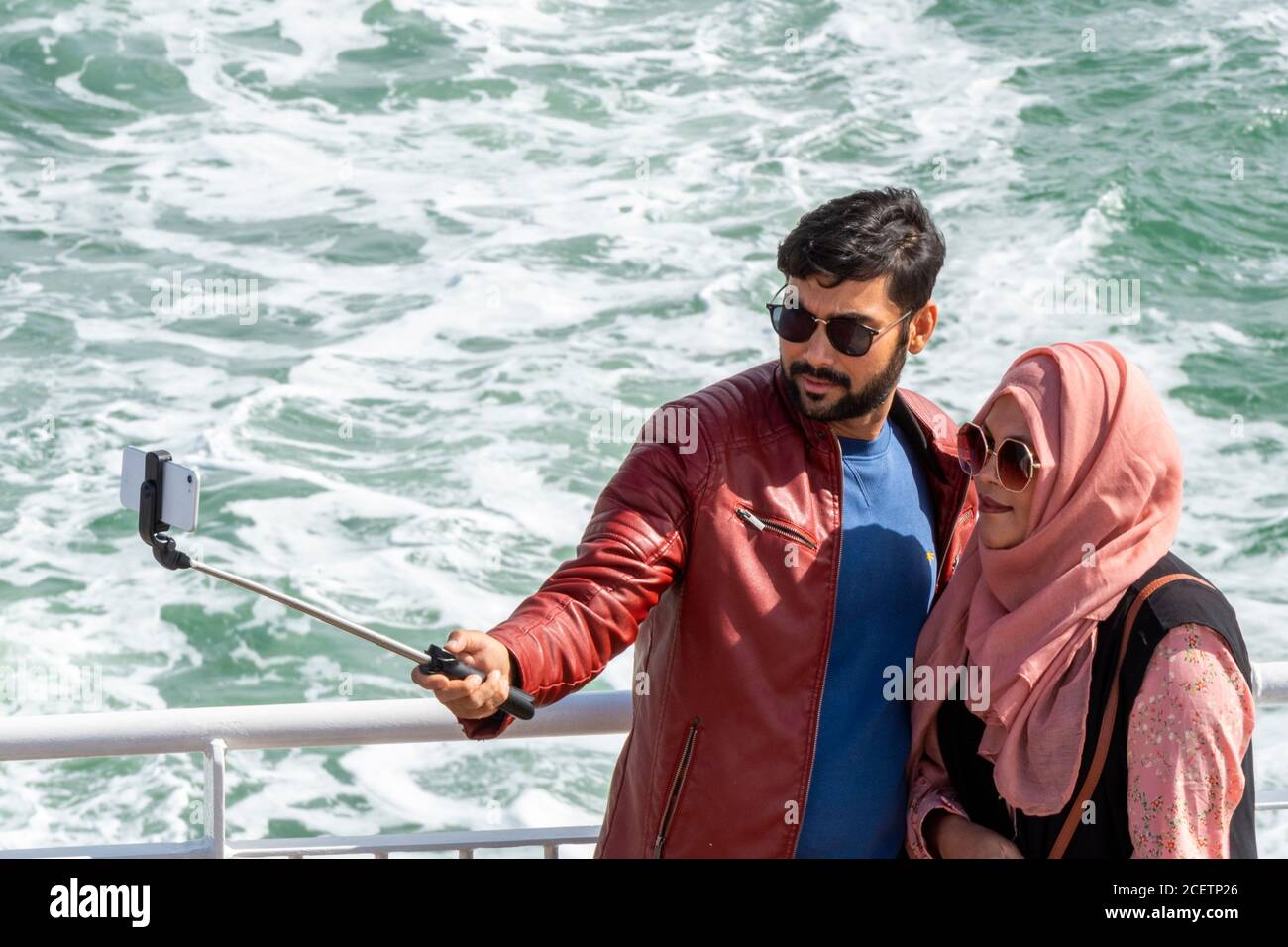 a young asian or ethnic bame couple on holiday taking a photgraph with ...