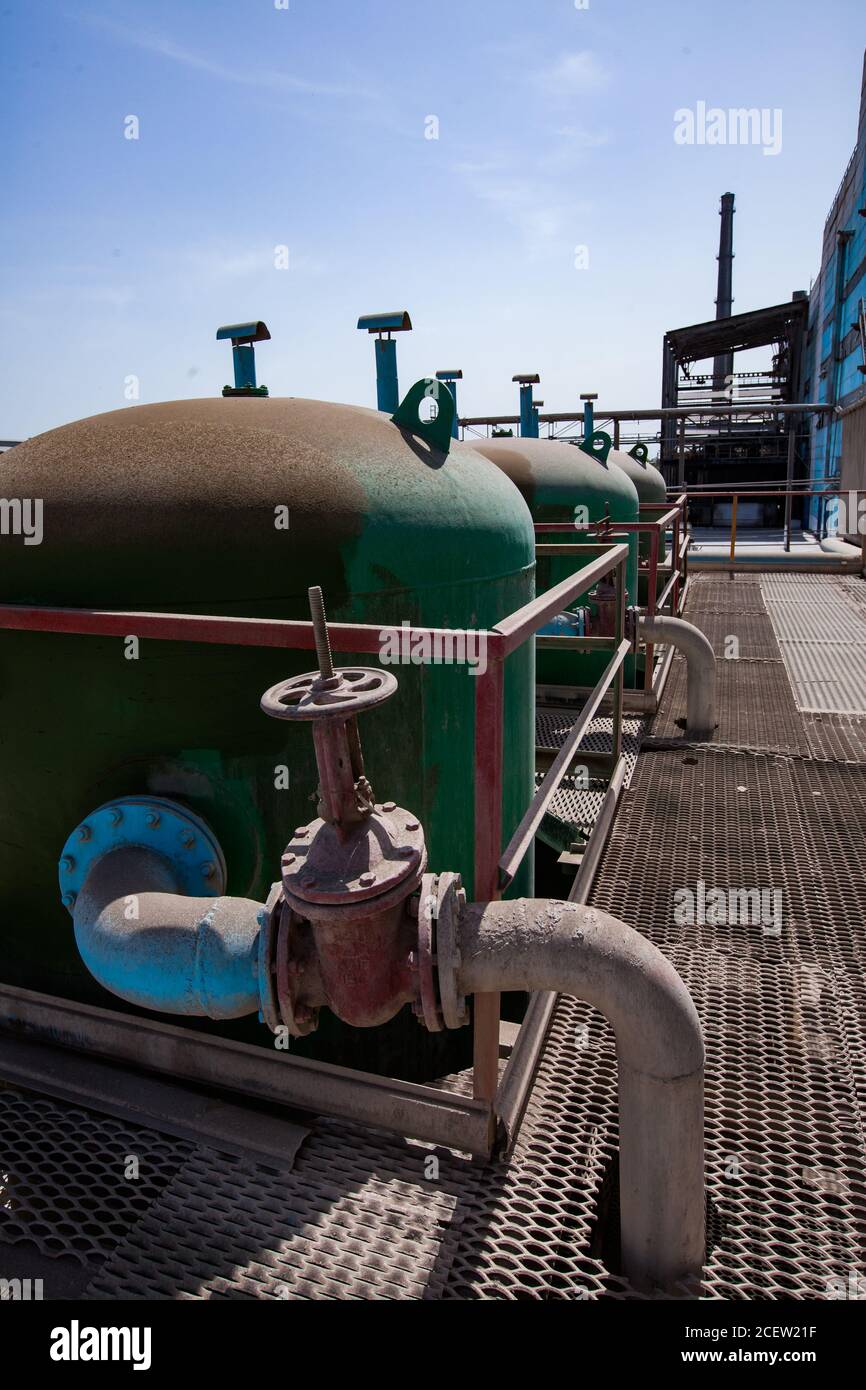 Some rusted metal tanks and valves and mesh floor on blue sky. Abstract ...