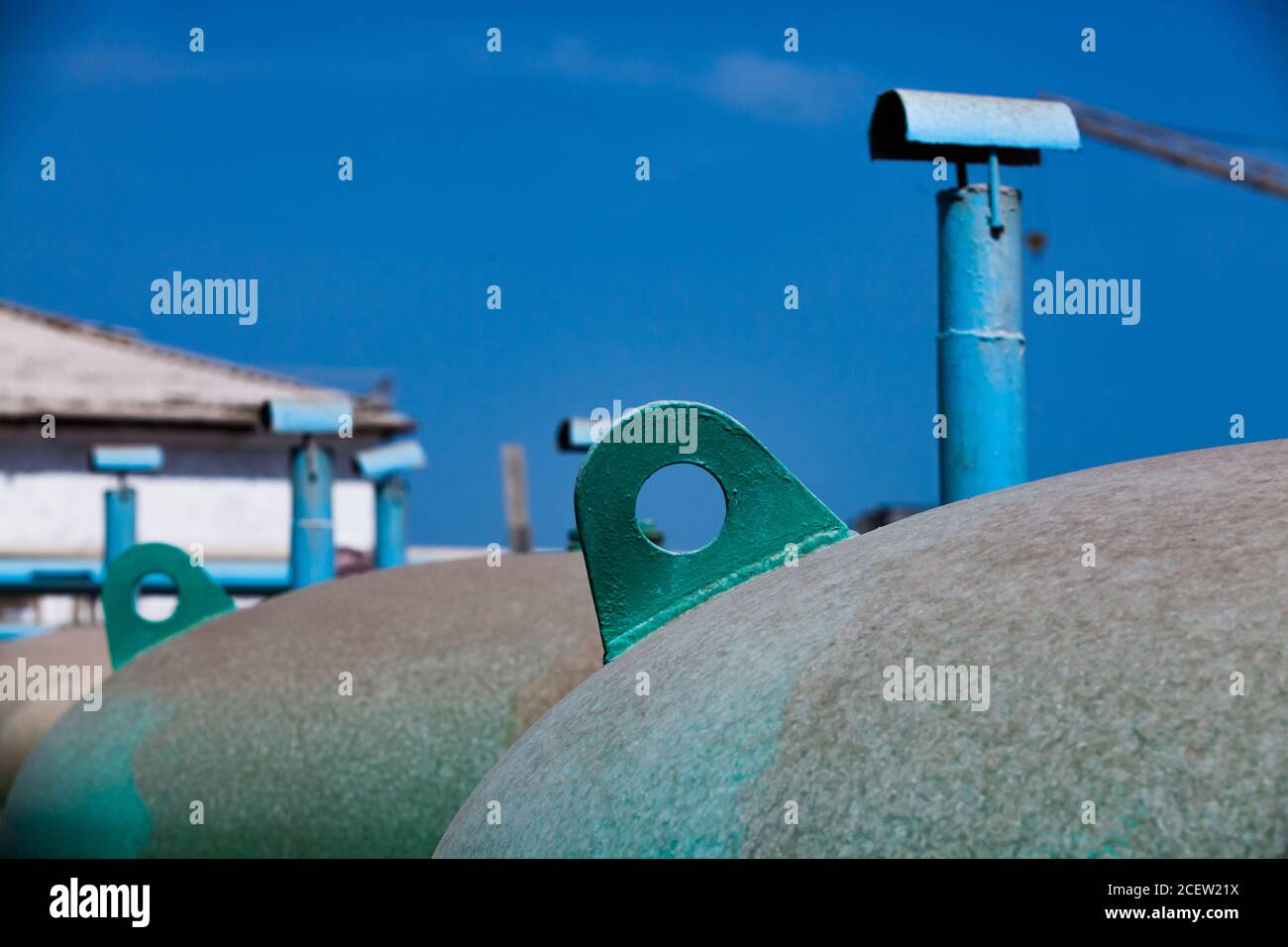Round green rusted iron storage tank and blue pipe on blue sky ...