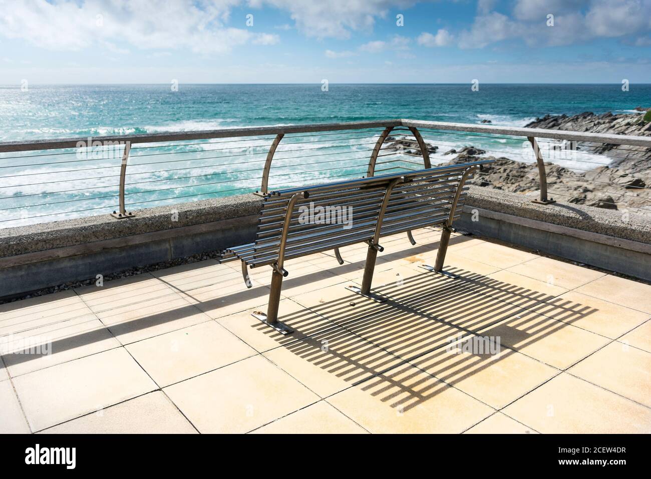 A metal bench casting a shadow on a balcony overlooking Fistral Beach ...
